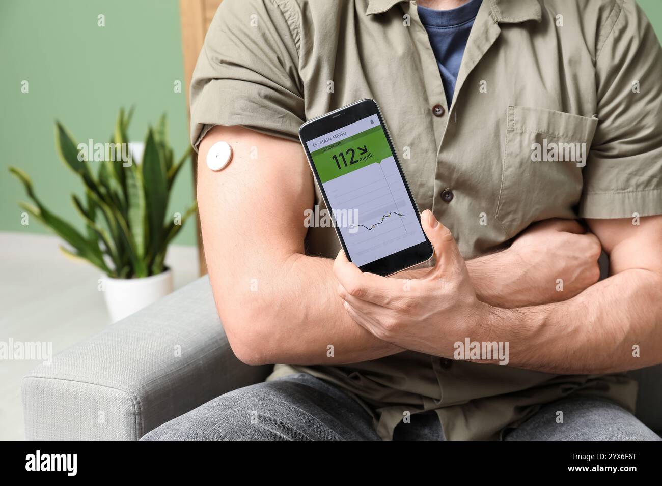 Diabetic young man with glucose sensor using mobile phone for measuring ...