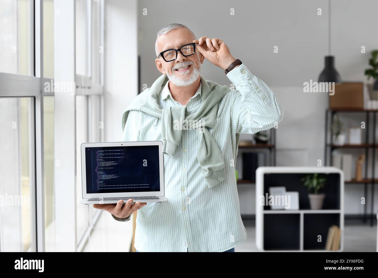 Mature programmer with laptop near window in office Stock Photo - Alamy