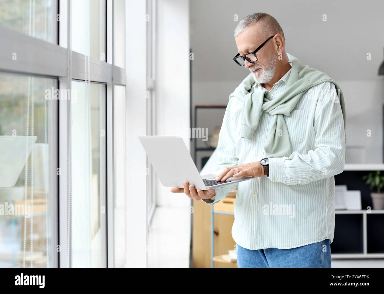 Mature programmer working with laptop near window in office Stock Photo ...