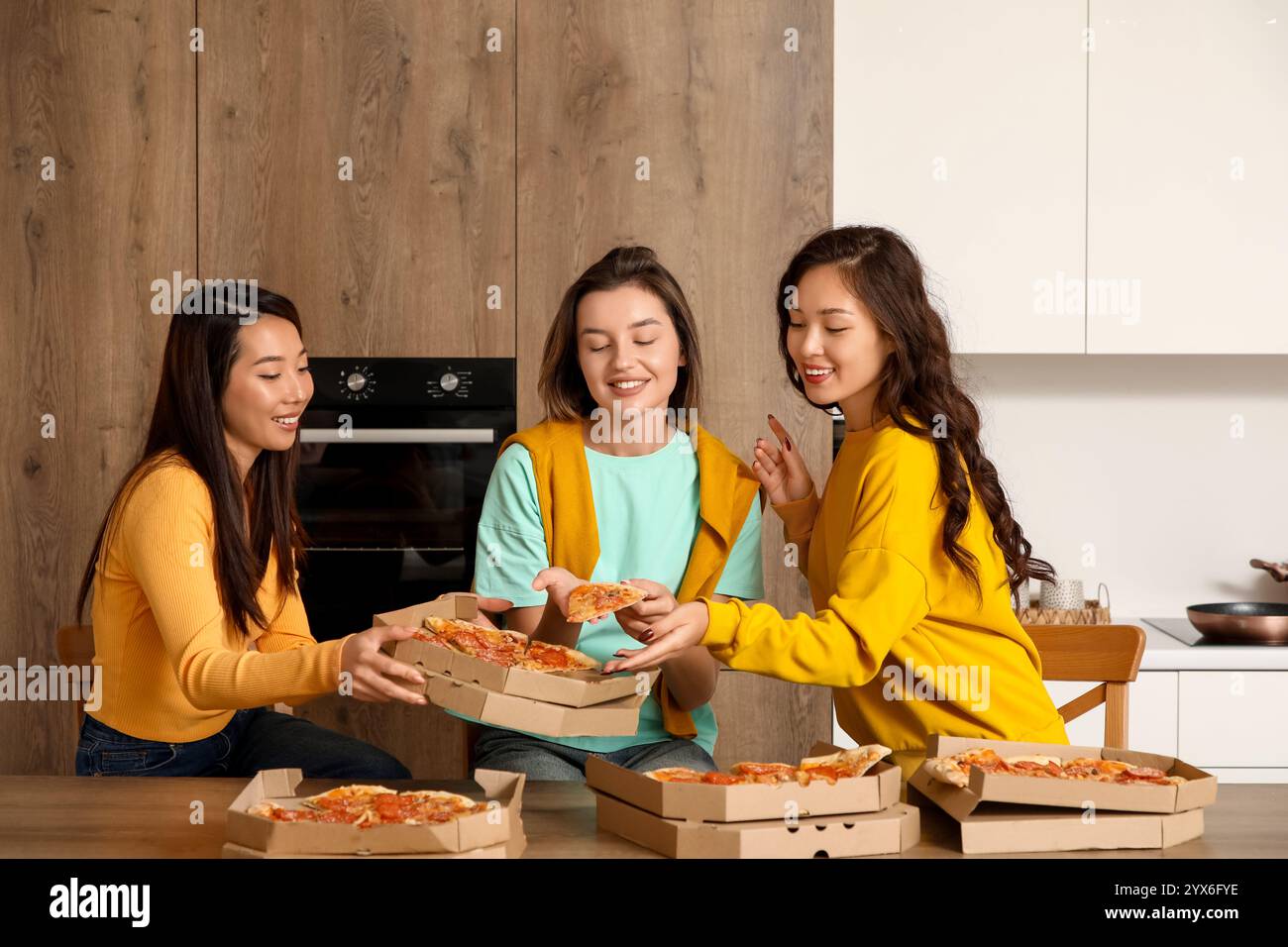 Female friends with tasty pepperoni pizza at table in kitchen Stock ...