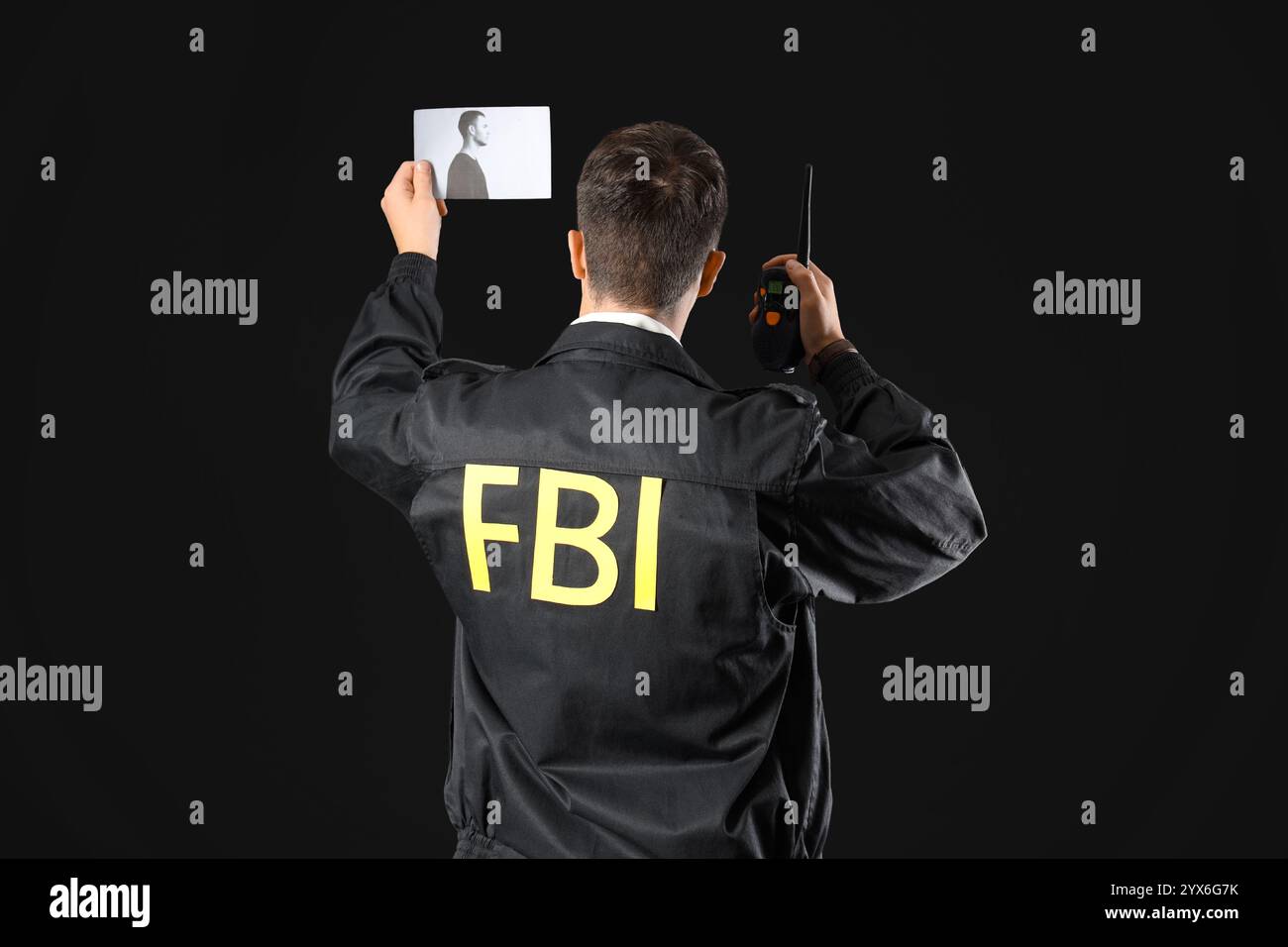 Male FBI agent with picture of suspect and two-way radio on dark ...