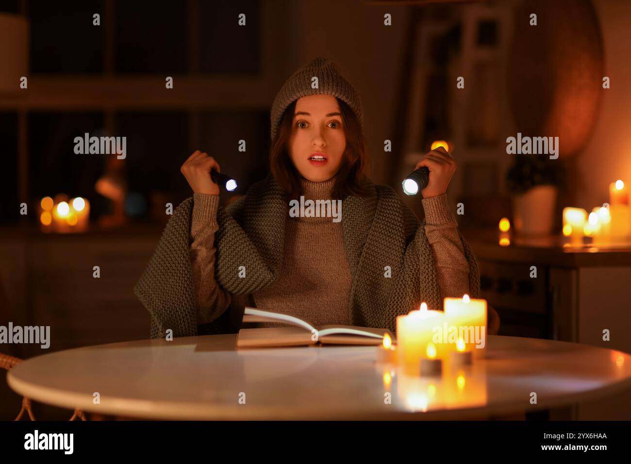 Shocked young woman with flashlights reading book at table in kitchen ...