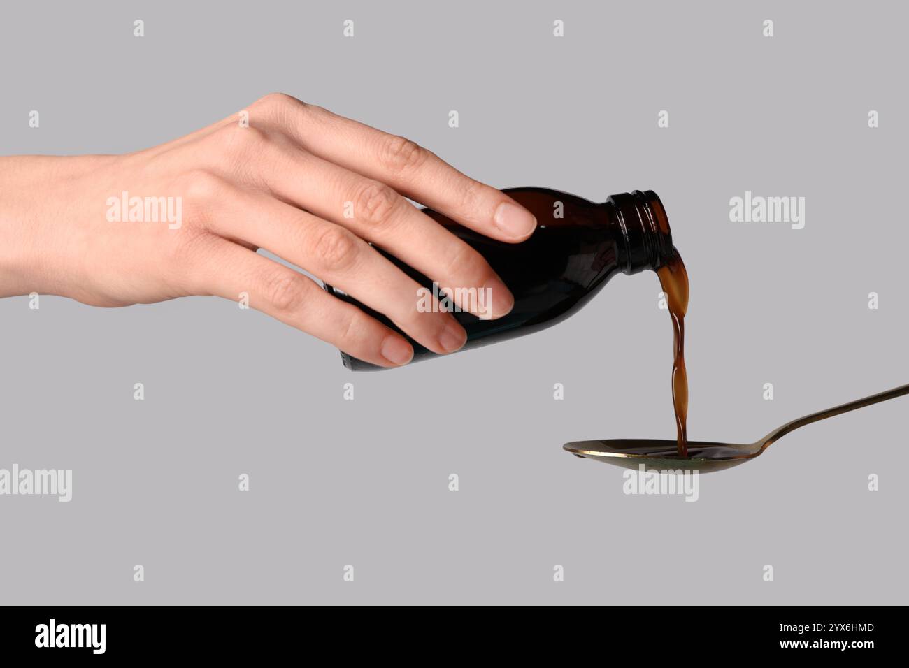 Woman pouring cough syrup from bottle into spoon on grey background ...