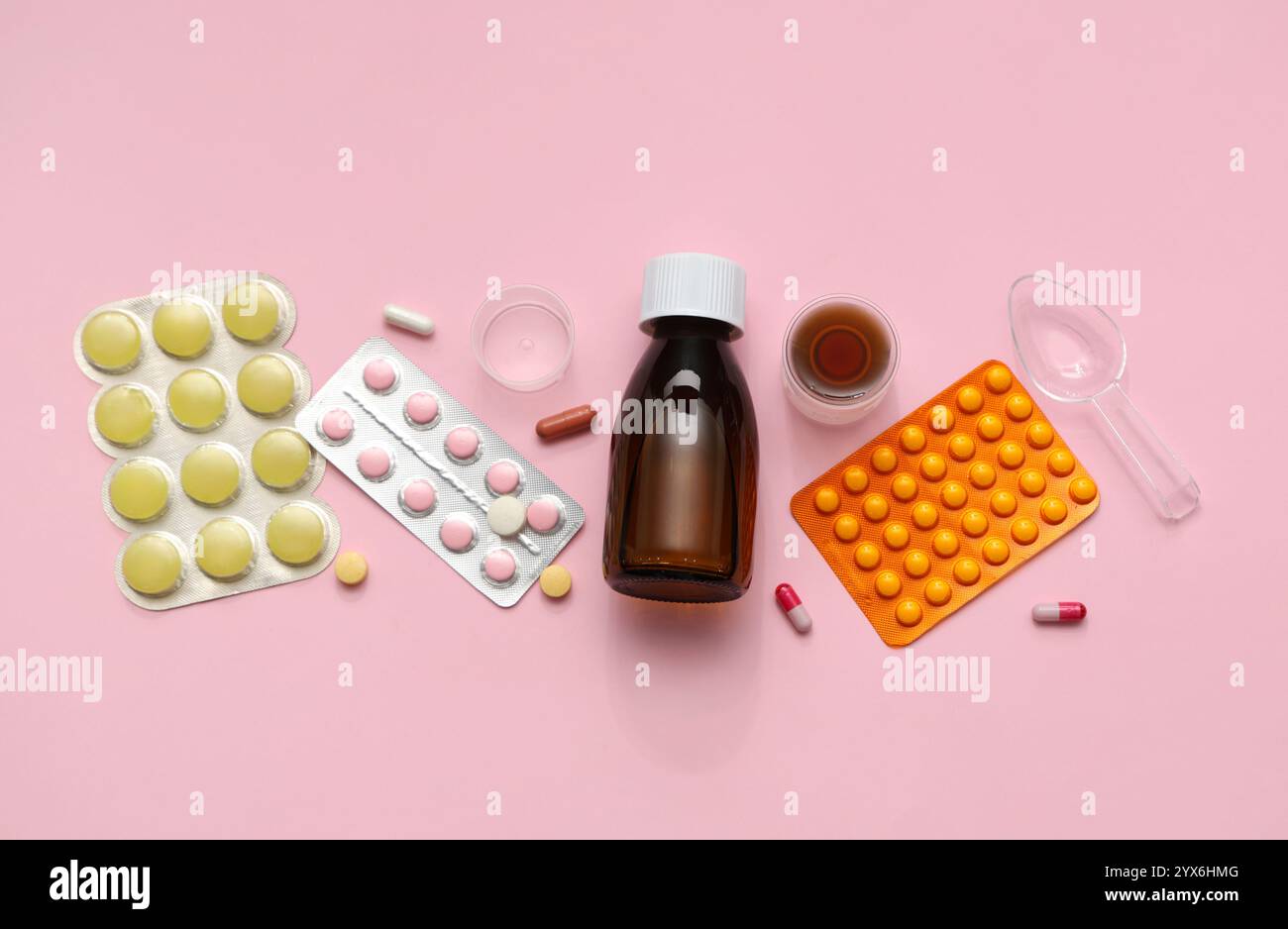 Bottle of cough syrup with measuring cups, spoon and different pills on ...
