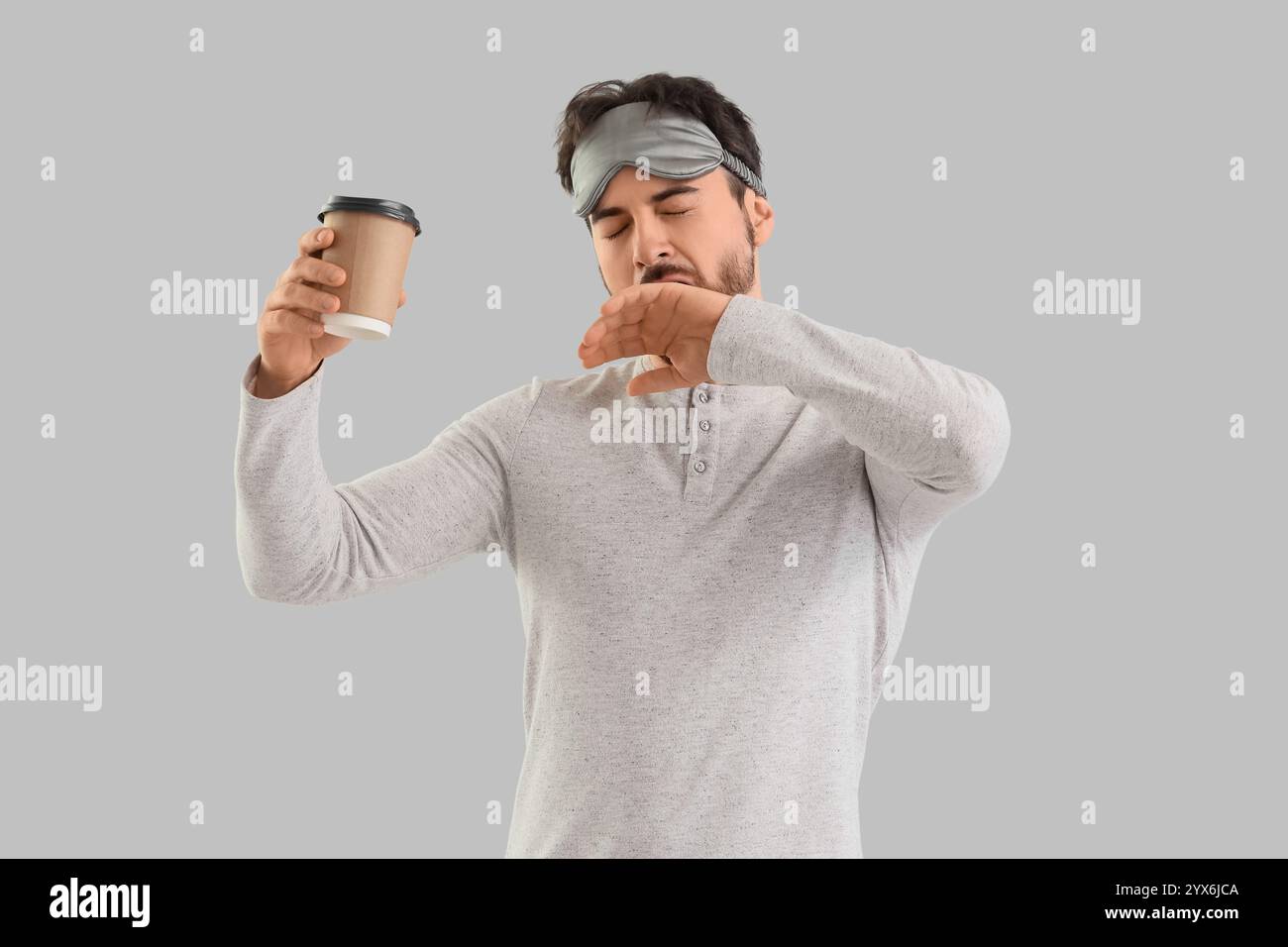 Sleepy young man with coffee cup yawning on light background Stock ...
