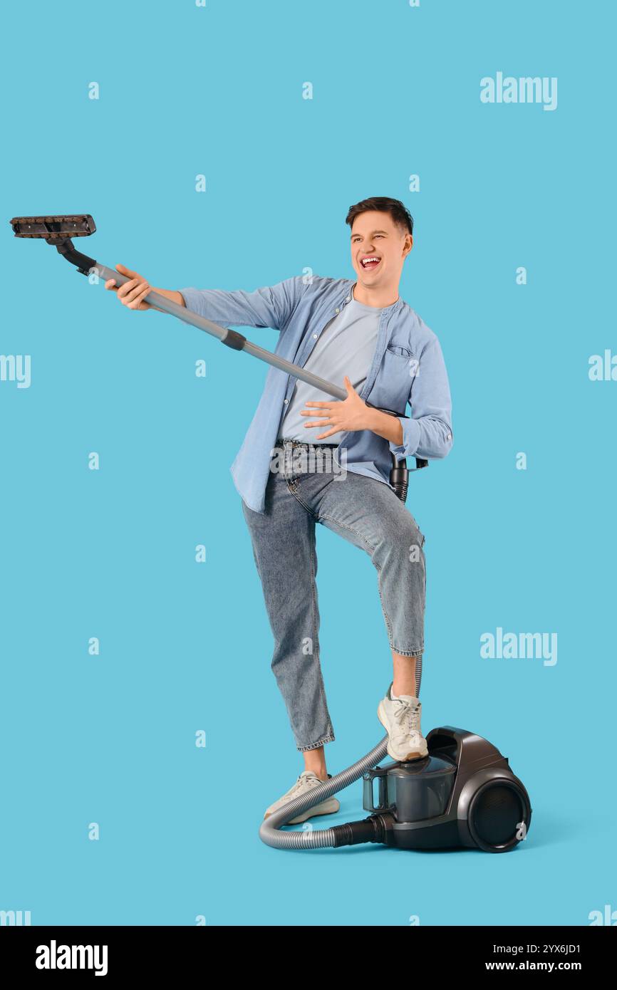 Young man with vacuum cleaner having fun on blue background Stock Photo ...
