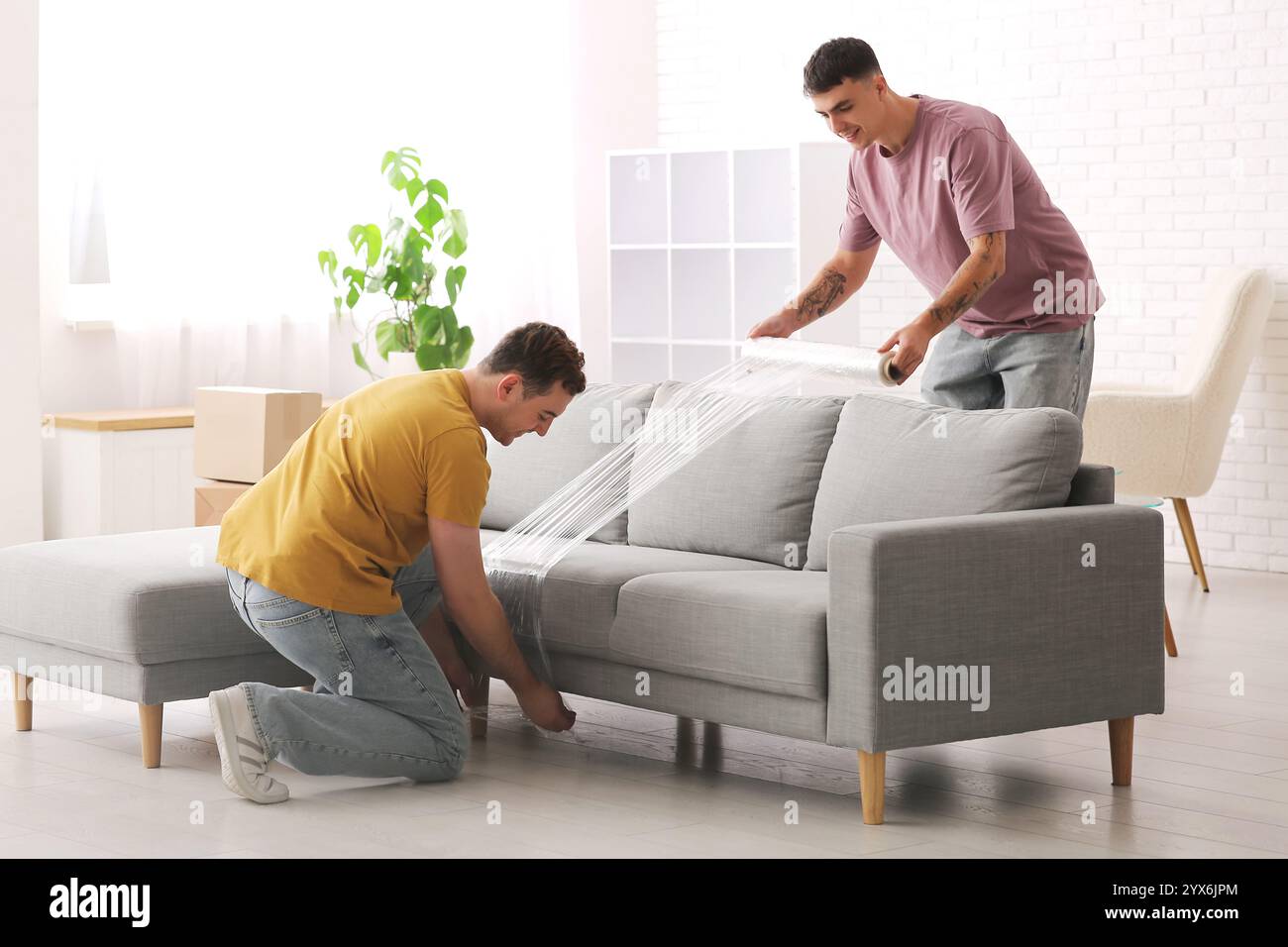 Young men wrapping sofa with stretch film in room on moving day Stock ...