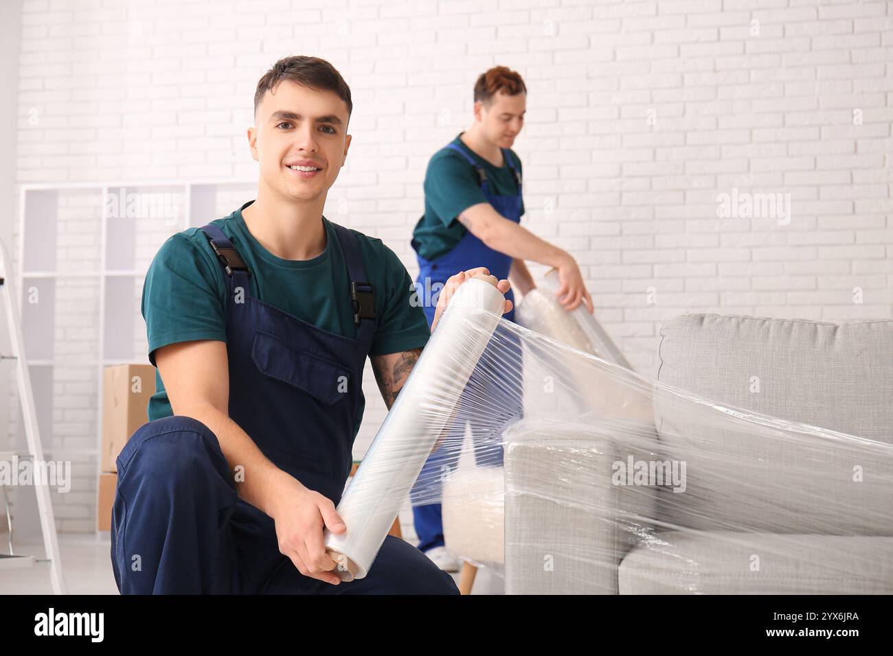 Male loader wrapping sofa with stretch film in room Stock Photo - Alamy