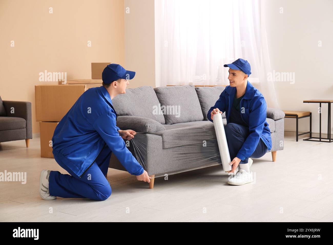 Male workers wrapping sofa with stretch film in room Stock Photo - Alamy