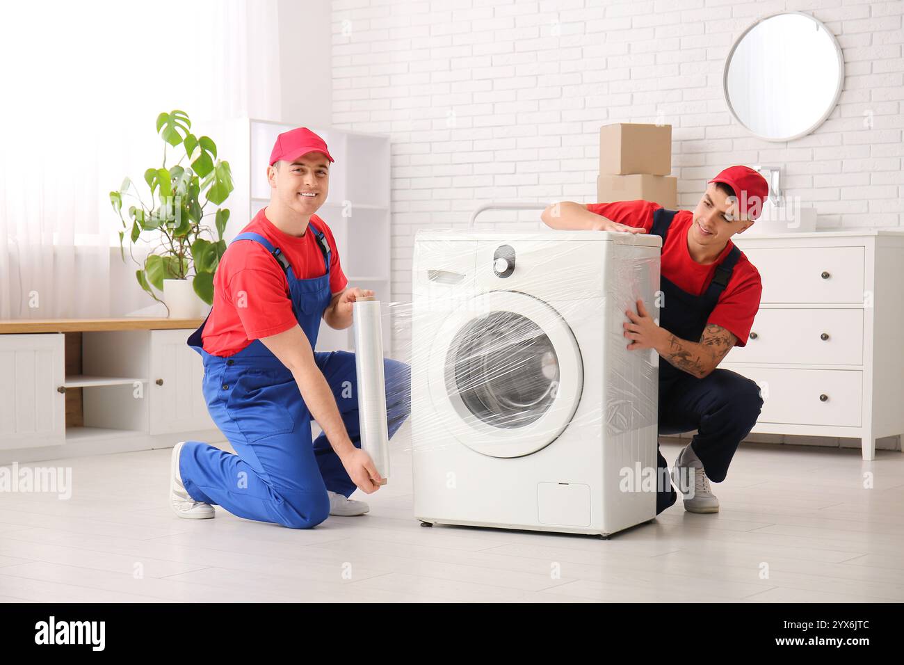 Male loaders wrapping washing machine with stretch film in room Stock ...
