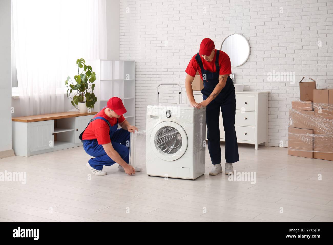 Male loaders wrapping washing machine with stretch film in room Stock ...