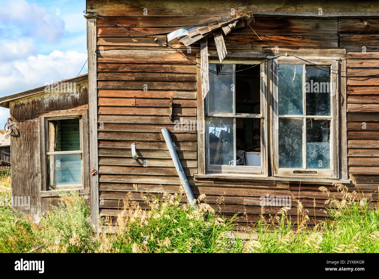A dilapidated old house with a broken window. The house is surrounded by weeds and grass Stock ...