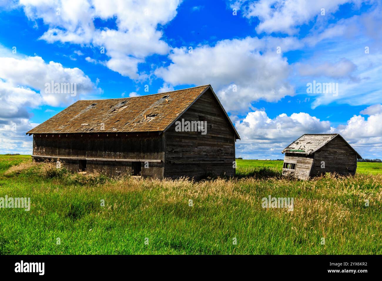 A large, old barn sits in a field with a cloudy sky overhead. The barn ...