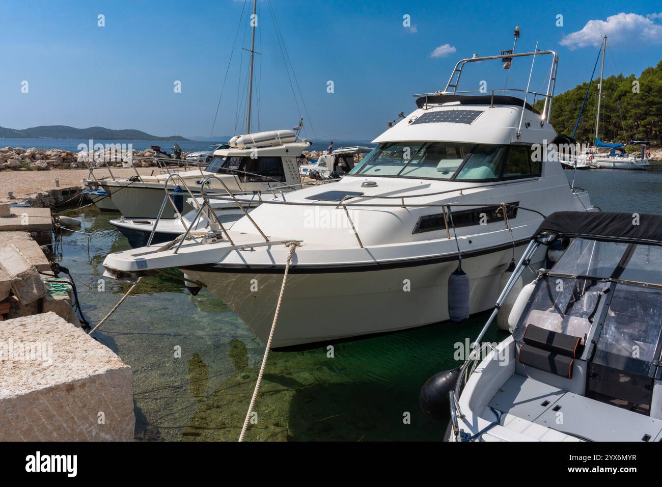 Elegant white motorboat anchored in quiet harbor with backdrop of lush ...