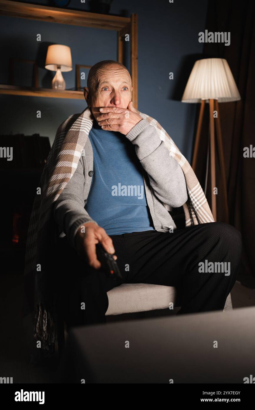 Shocked elderly man holding remote controller sitting in armchair ...