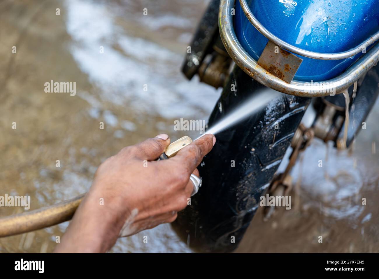 Close-up of hand washing a muddy motorcycle tire with water hose ...