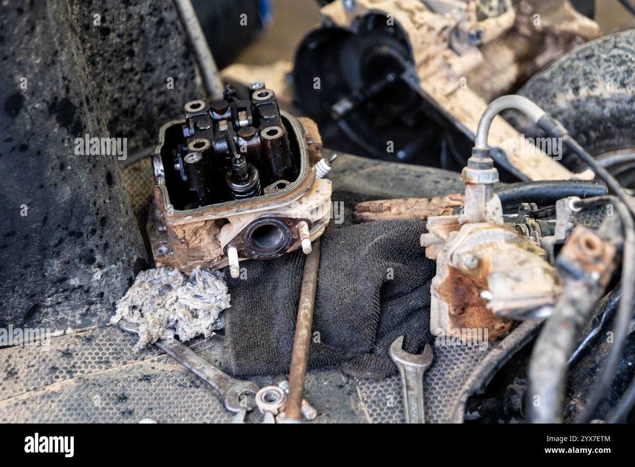 Disassembled engine parts, wrenches, and a dirty rag lay on a textured ...