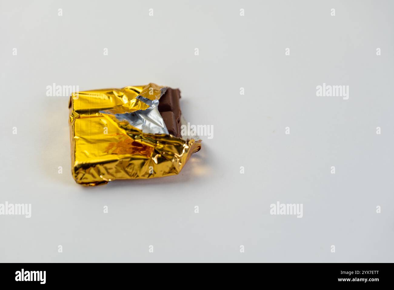 A partially unwrapped chocolate square in gold foil, a sweet treat ...