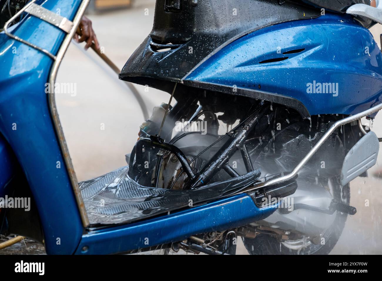 A blue scooter gets a thorough cleaning, water cascading over its frame ...