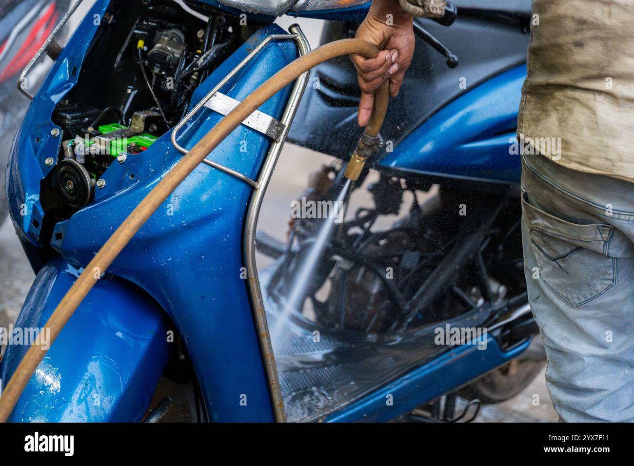 Man washing a blue scooter engine with water hose. Close-up, cleaning ...