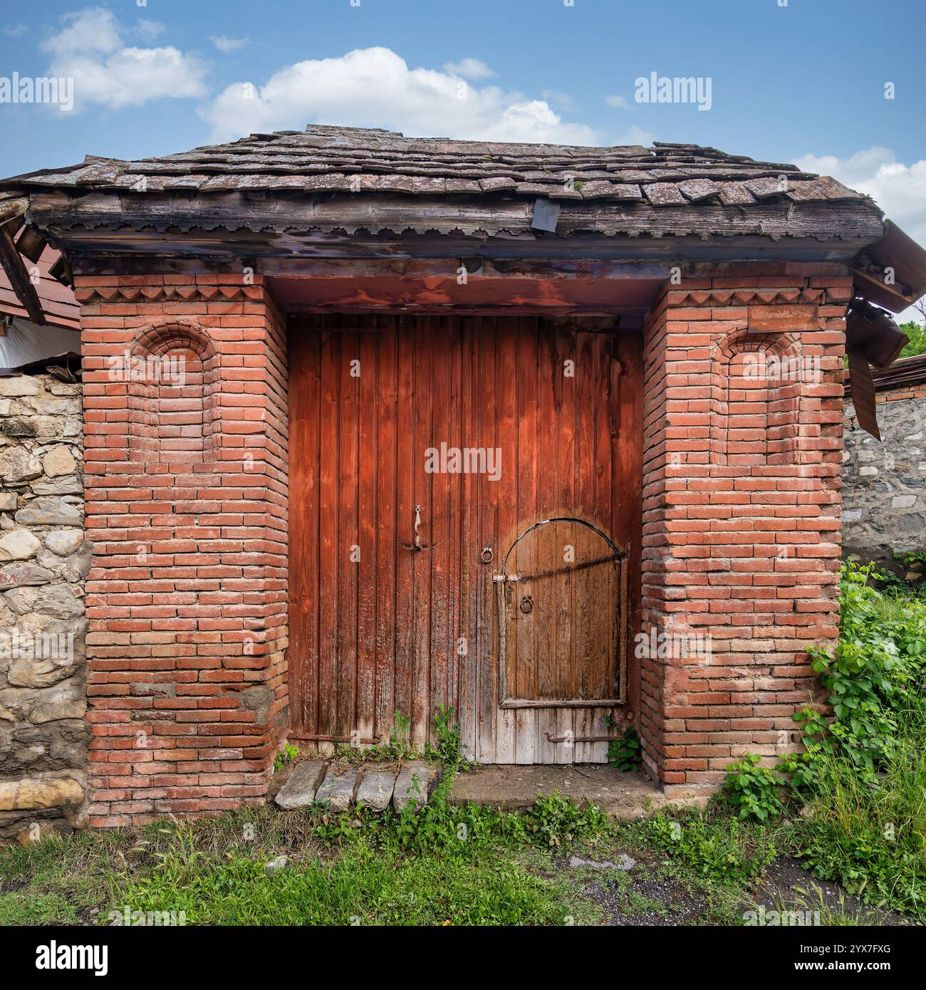 A rustic brick structure with a vibrant red wooden door captures the ...