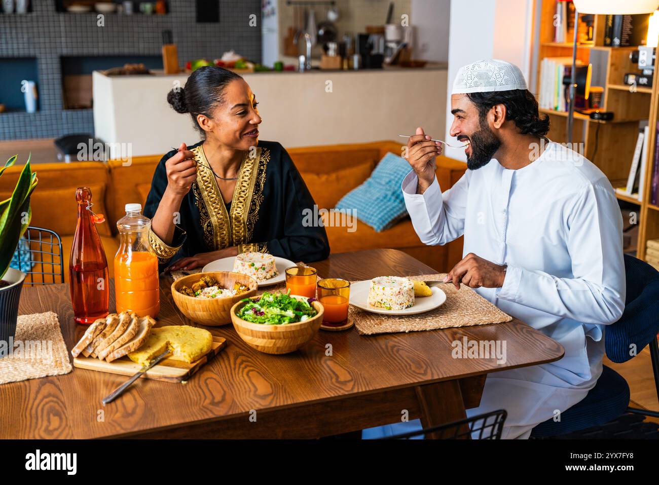 Happy beautiful young arab couple with emirati clothing having lunch together at home - Middle ...