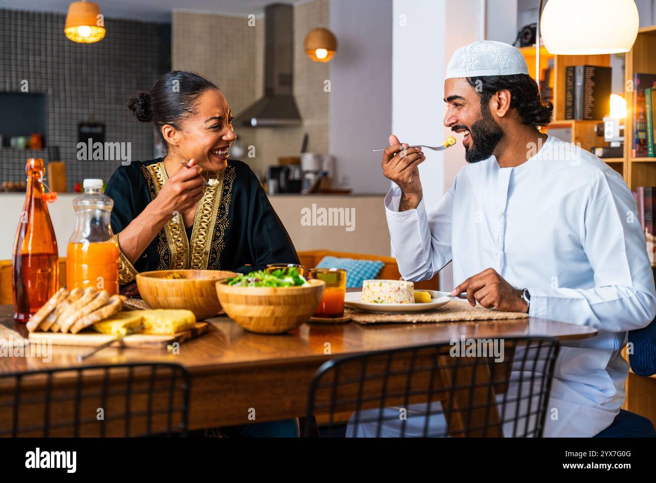 Happy beautiful young arab couple with emirati clothing having lunch together at home - Middle ...