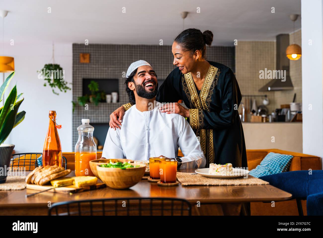 Happy beautiful young arab couple with emirati clothing having lunch together at home - Middle ...