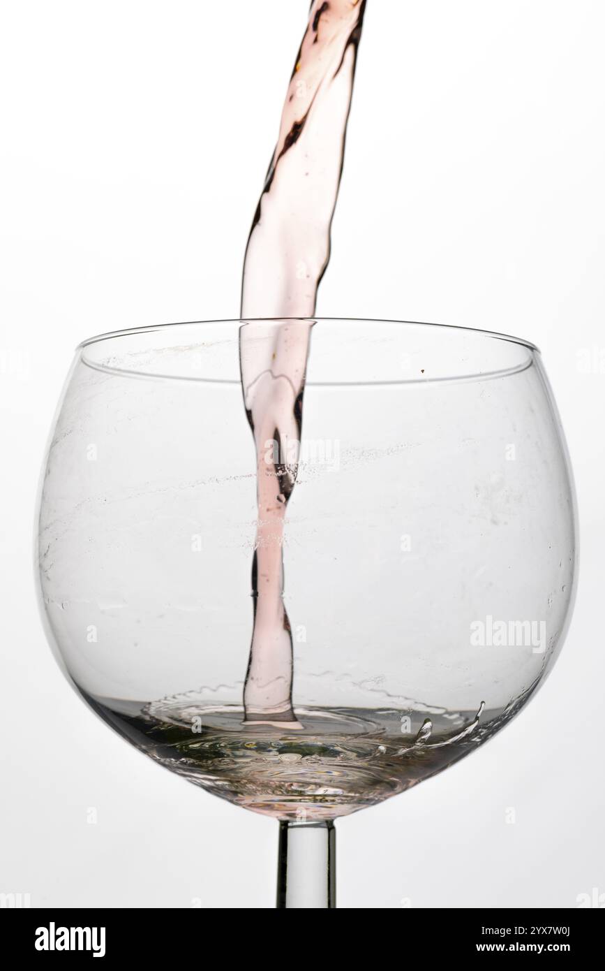 Rose-coloured liquid is poured into a transparent glass and creates ...