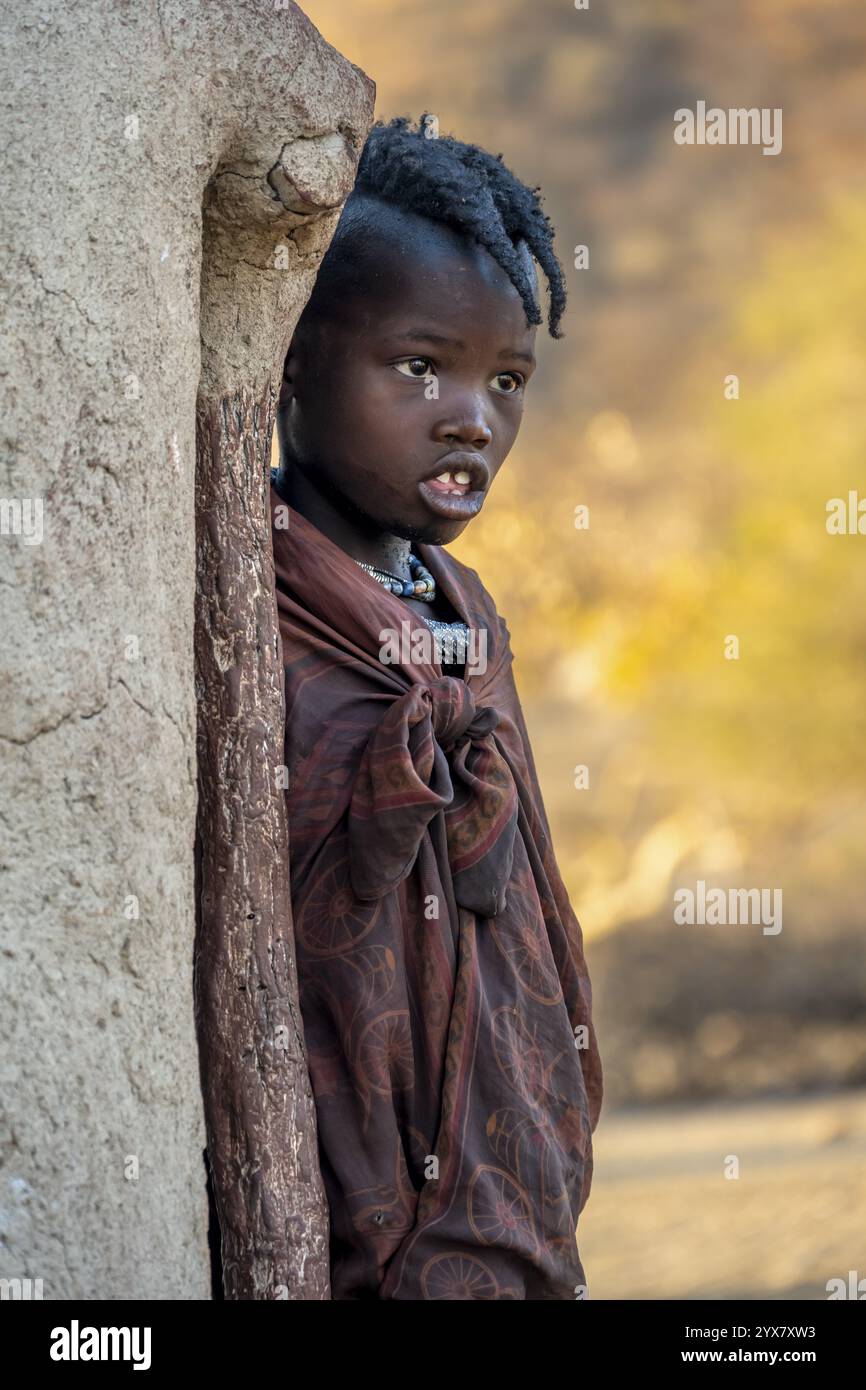 Himba girl leaning against a traditional mud hut, in the morning ...