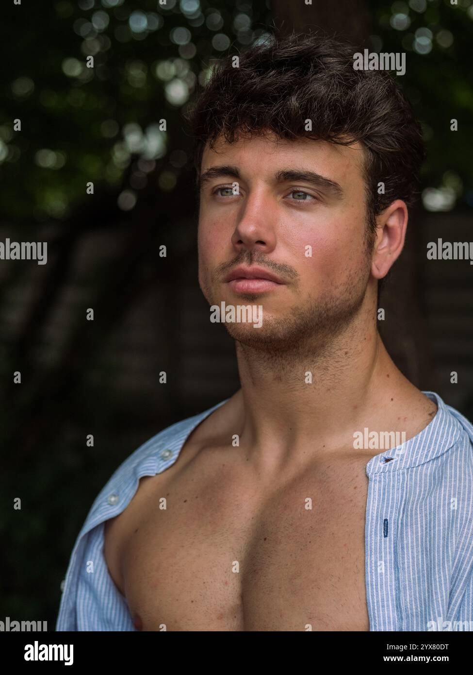 A young male model with curly hair and a thoughtful expression stands ...