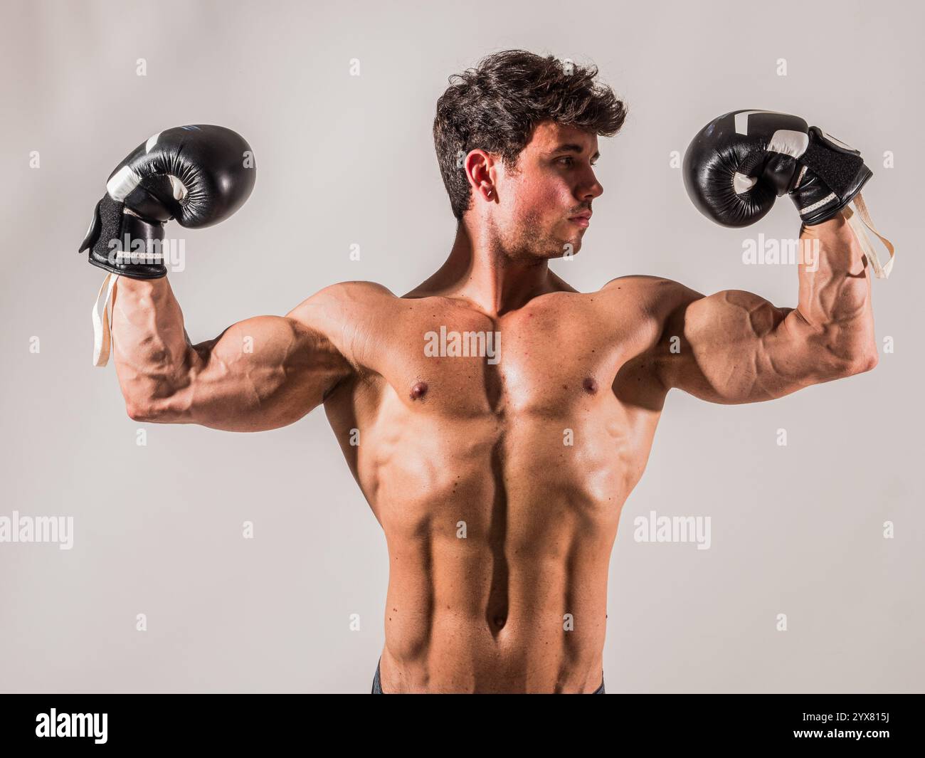 A muscular male athlete flexes his biceps while wearing black boxing ...