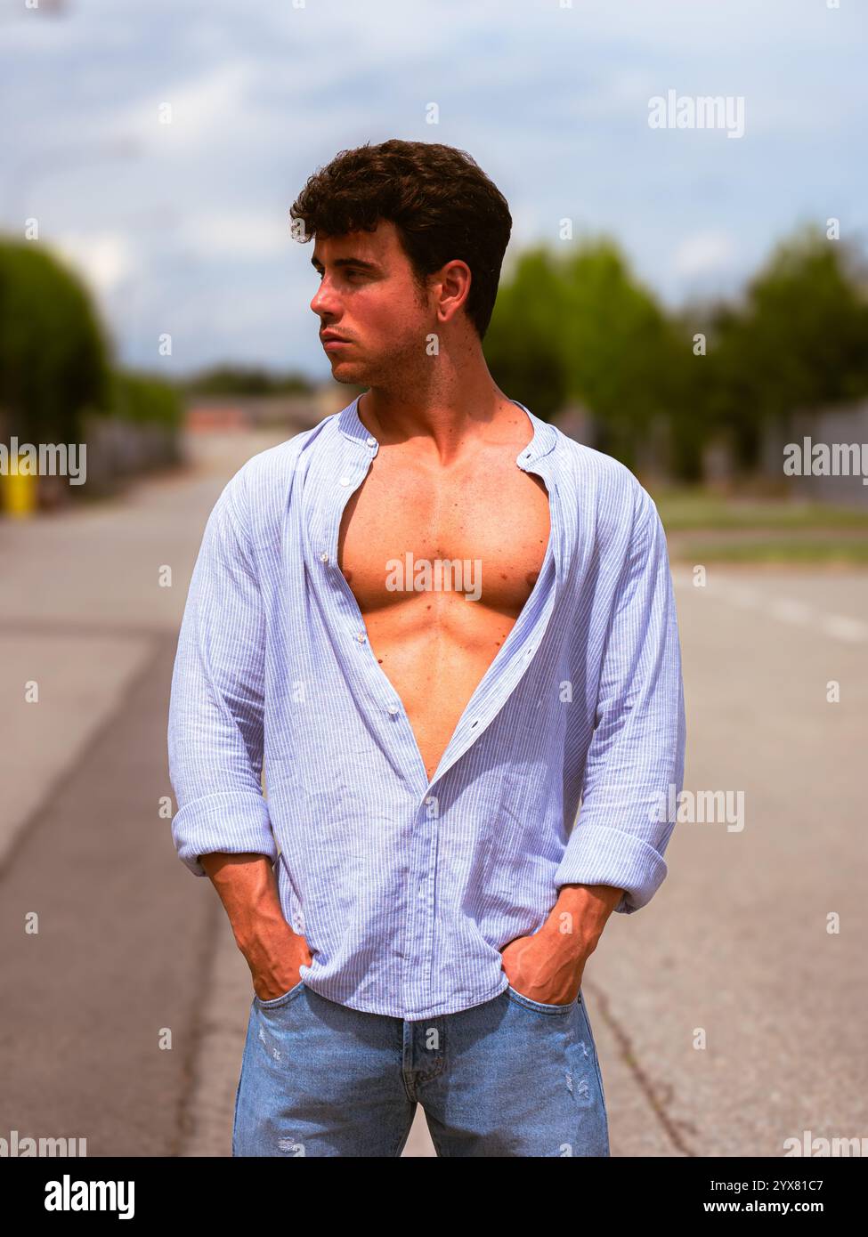 A young man stands confidently on a vacant street, wearing a light blue ...