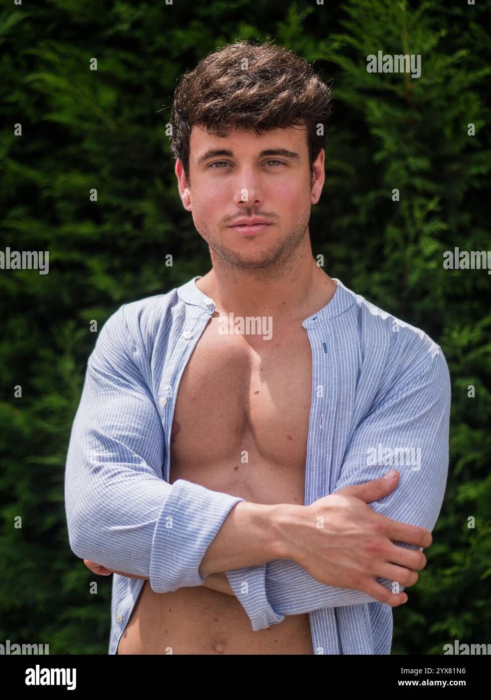 A young man stands with his arms crossed outside, showcasing his casual ...