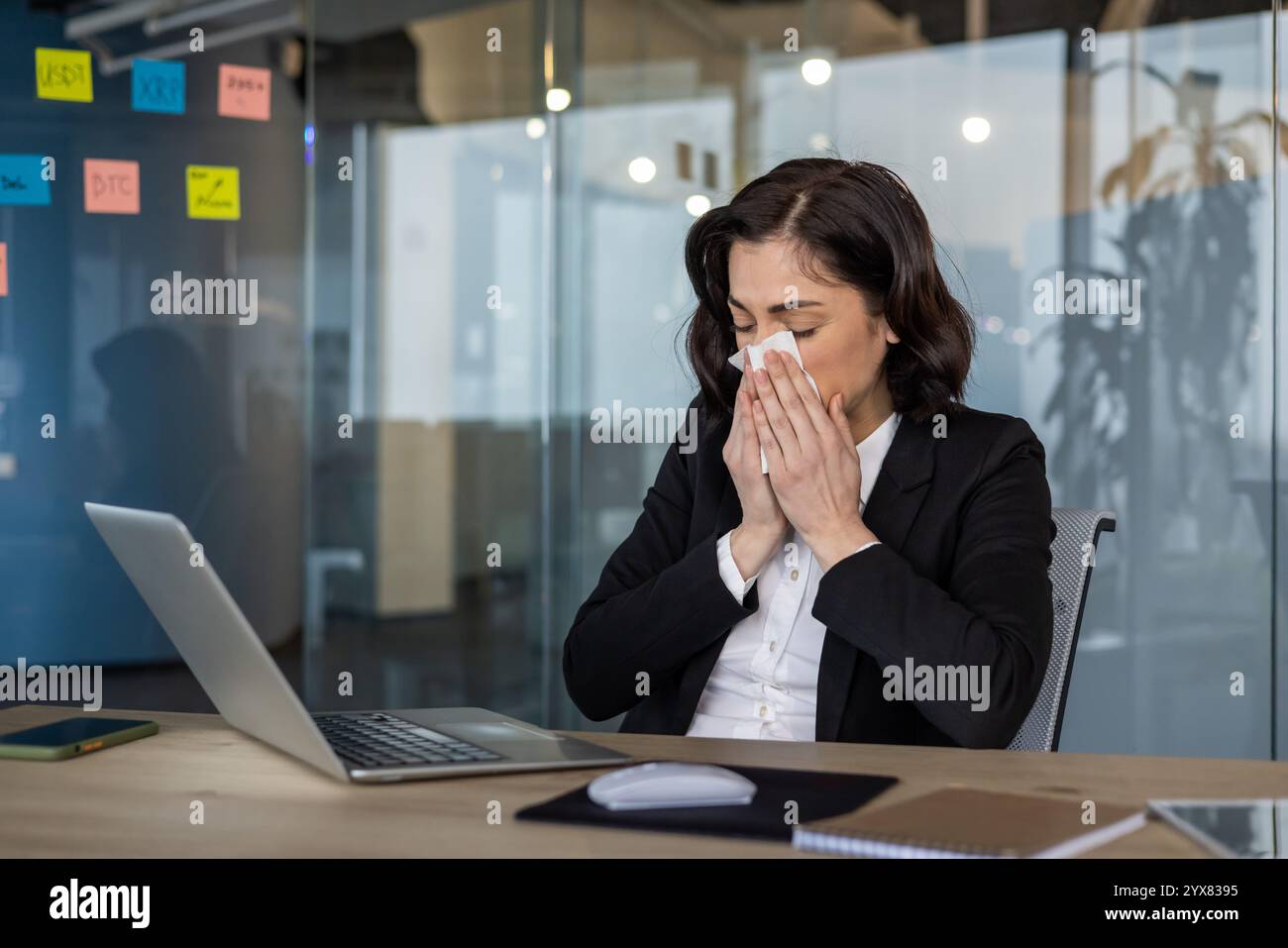Businesswoman sneezing at office desk with laptop open, showing ...