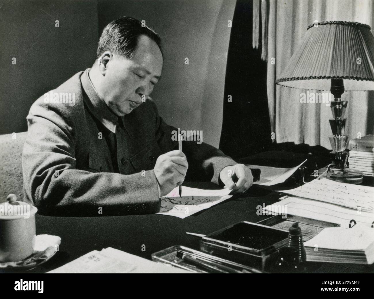 Mao Zedong writing at a desk in a dimly lit room during the mid-20th ...
