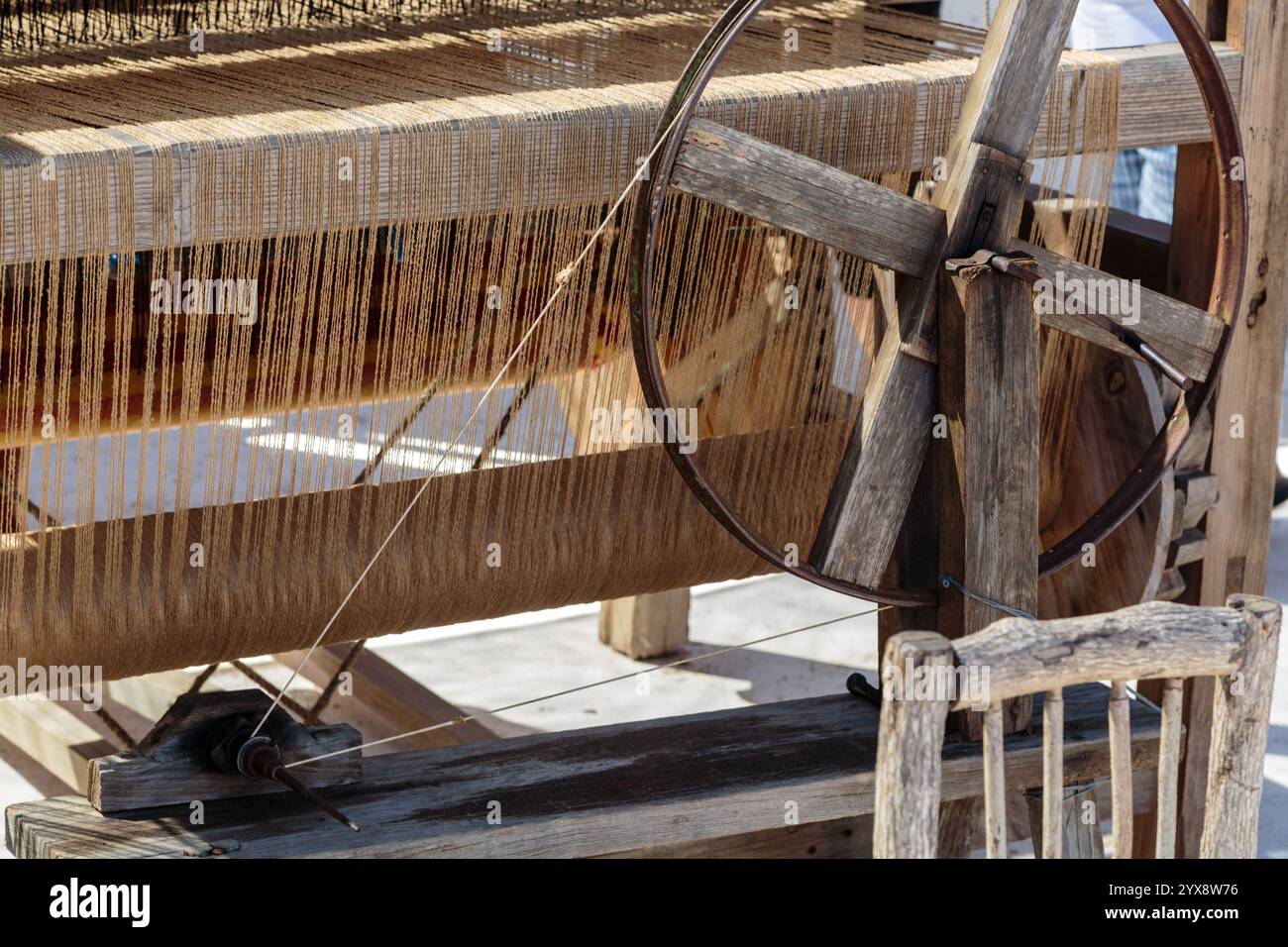 A wooden spinning wheel sits on a table next to a chair. The wheel is ...