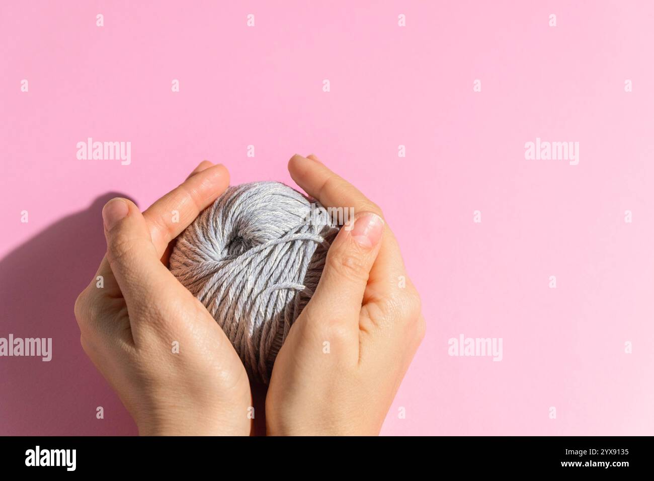 Hands holding ball of wool yarn on light pink background, copy space ...