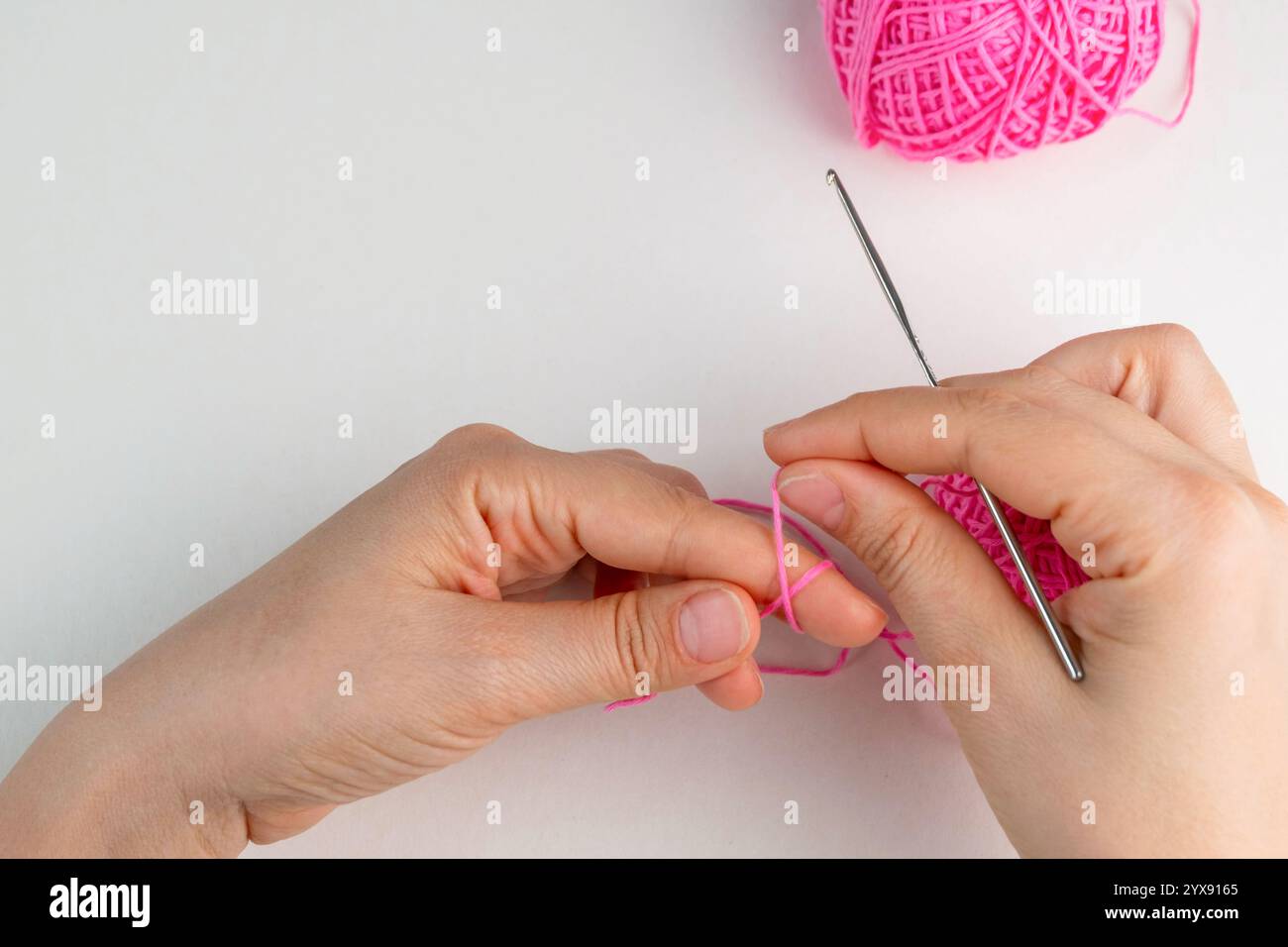 Hand holding thread of pink yarn and a chrocket hook on light ...