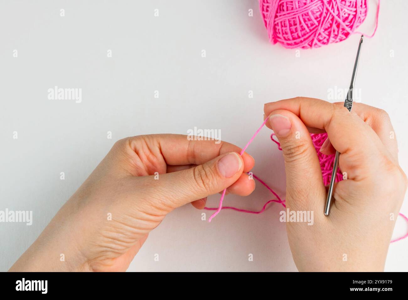 Hand holding thread of pink yarn and a chrocket hook on light ...
