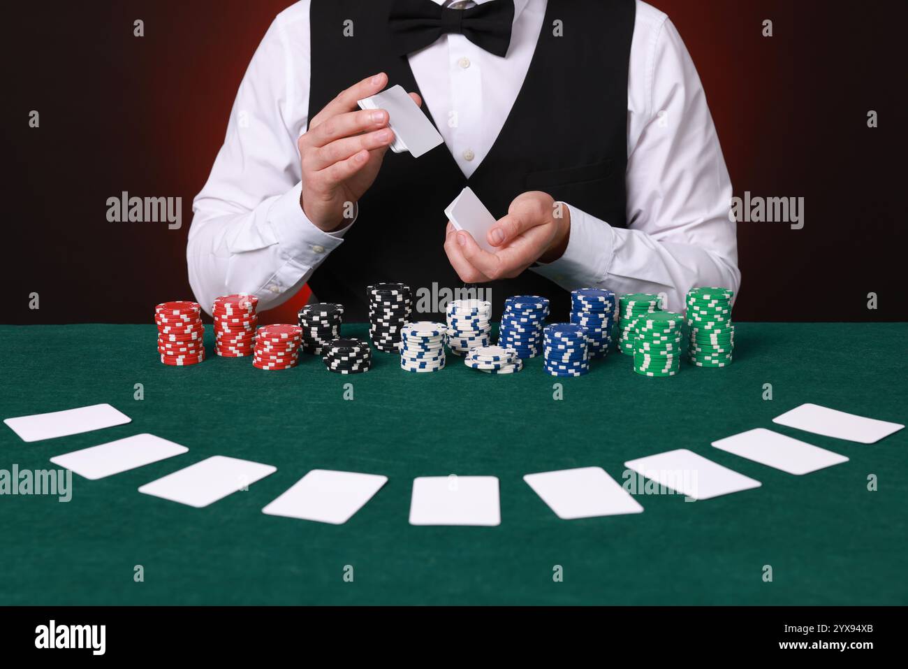 Professional croupier shuffling cards at gambling table against dark ...