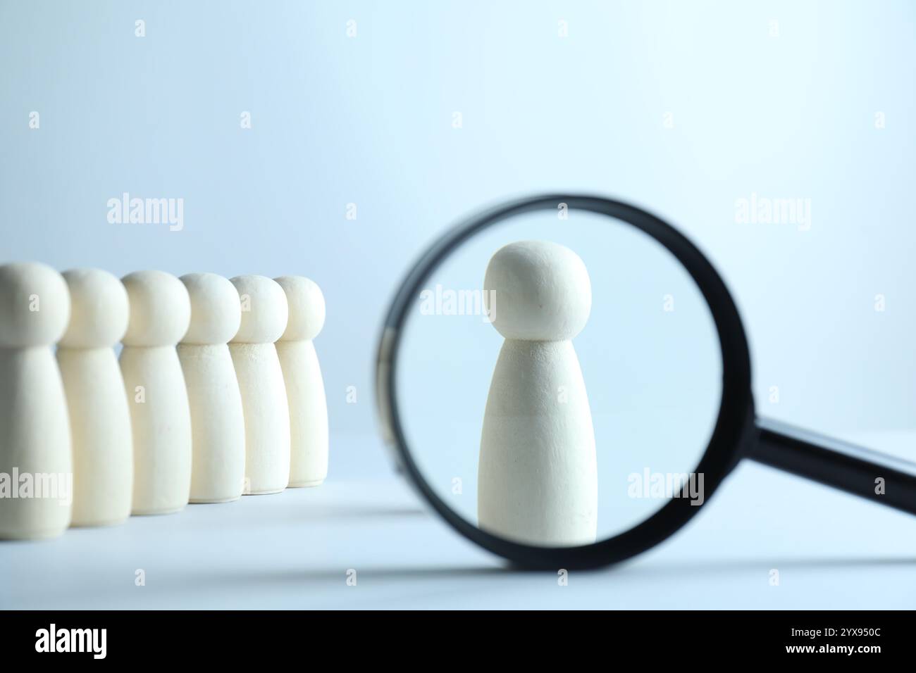 Human resources concept. Looking at wooden figure through magnifying glass on light background ...