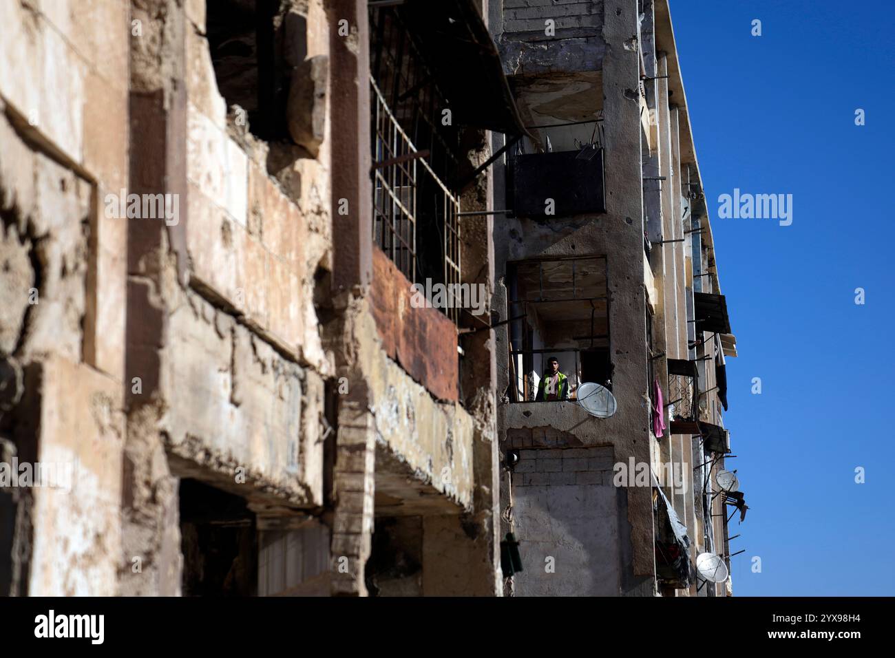 A Syrian boy looks on from the balcony of a house in a partially ...