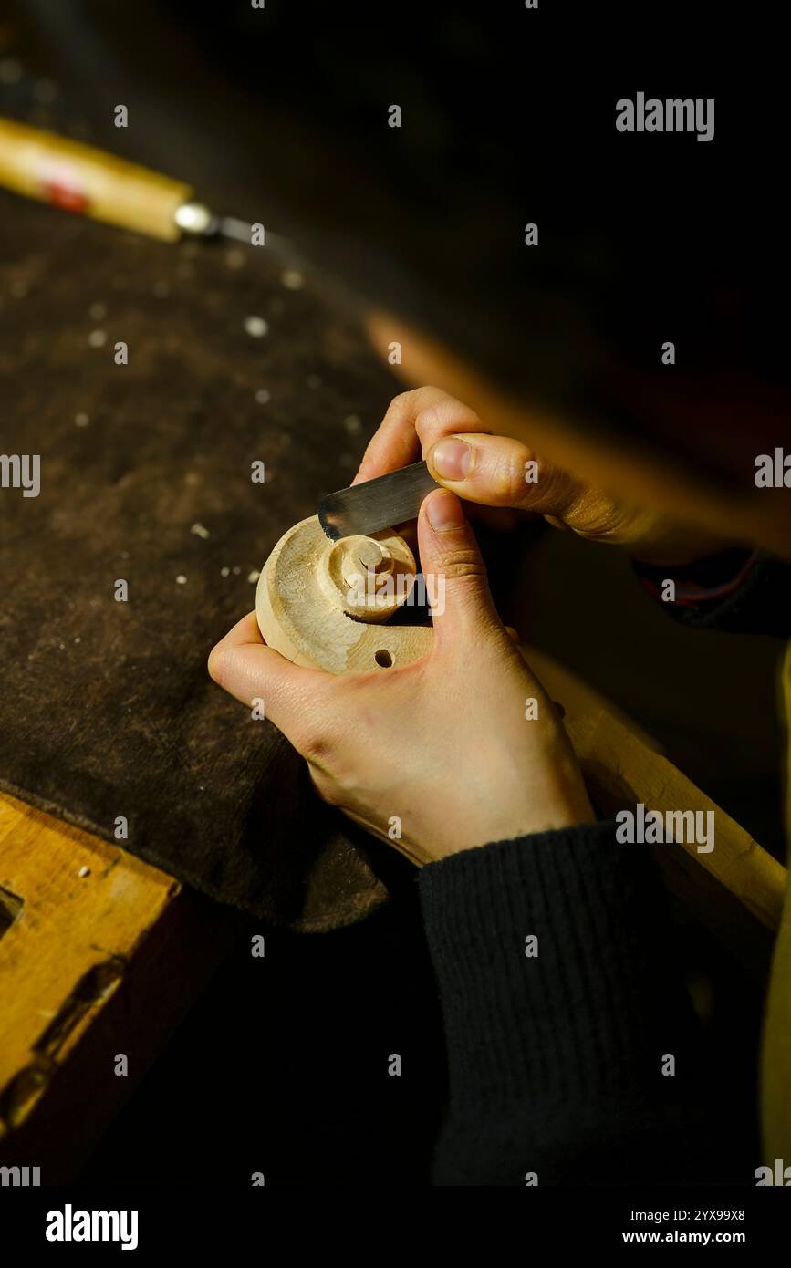 Female luthier meticulously carving a violin scroll using a small ...