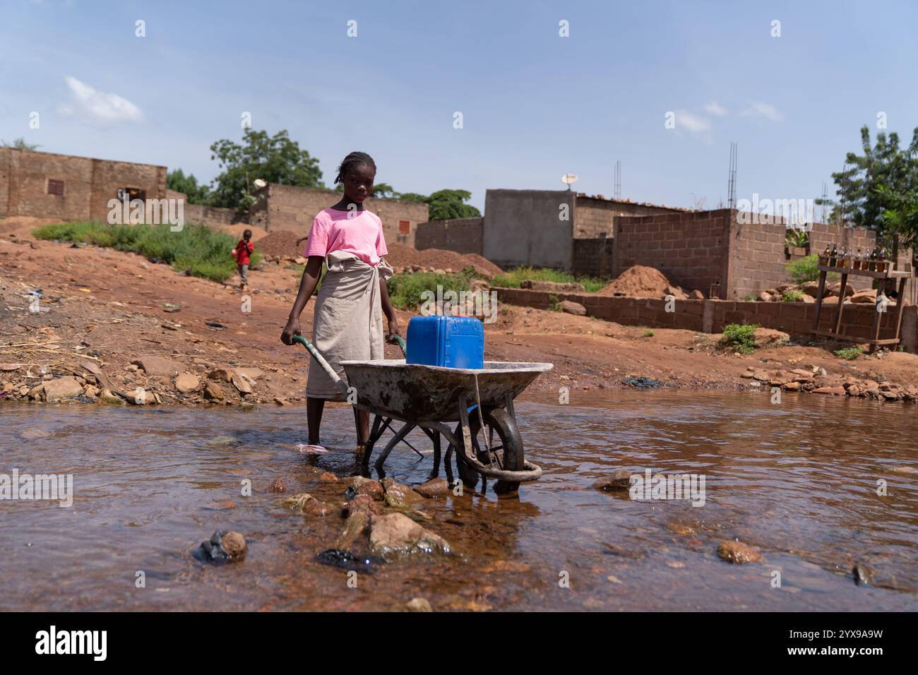 Rural scene of a young African child wading through a river with her ...