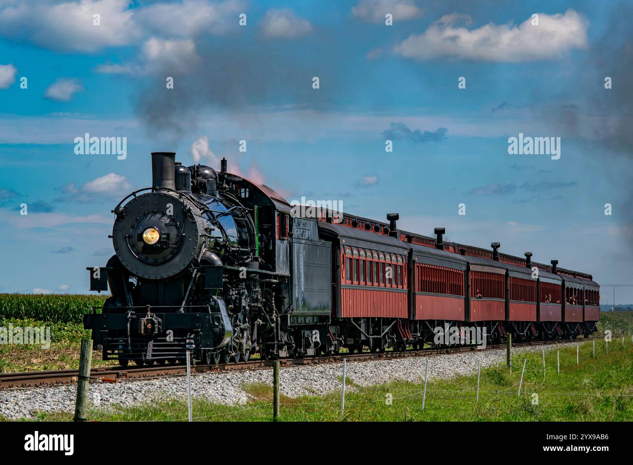 A classic steam train chugs along the tracks, billowing smoke into the ...