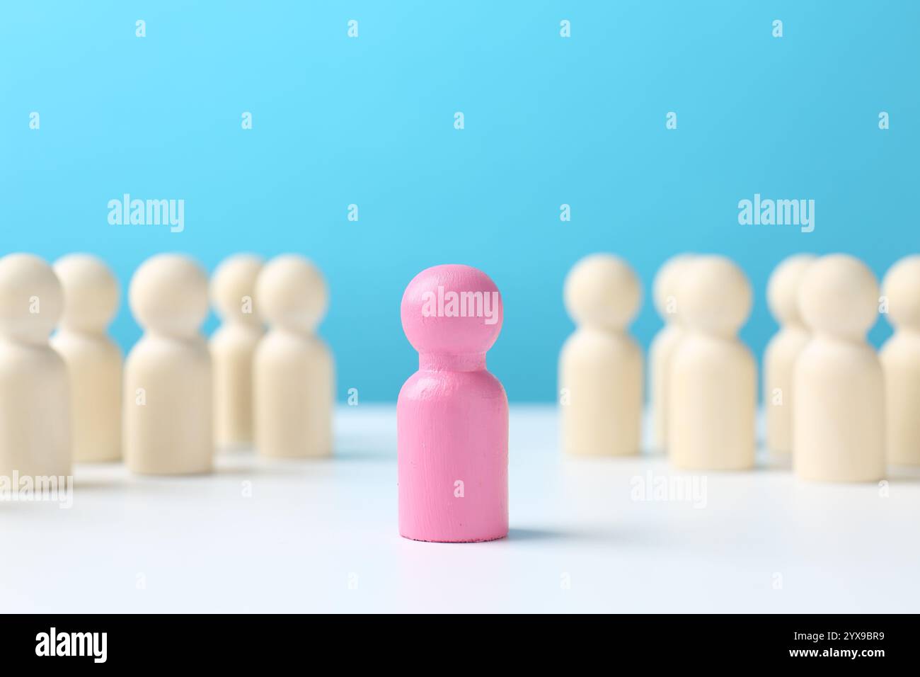 Pink figure among white ones on table against light blue background ...