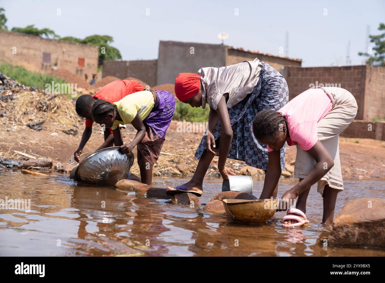 Group of West African village girls washing dishes in the stagnant ...