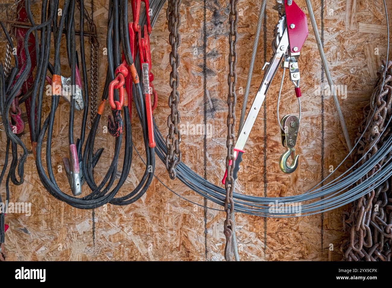 Electrical cables, chains, and a metal hook are hanging on a wall in a ...