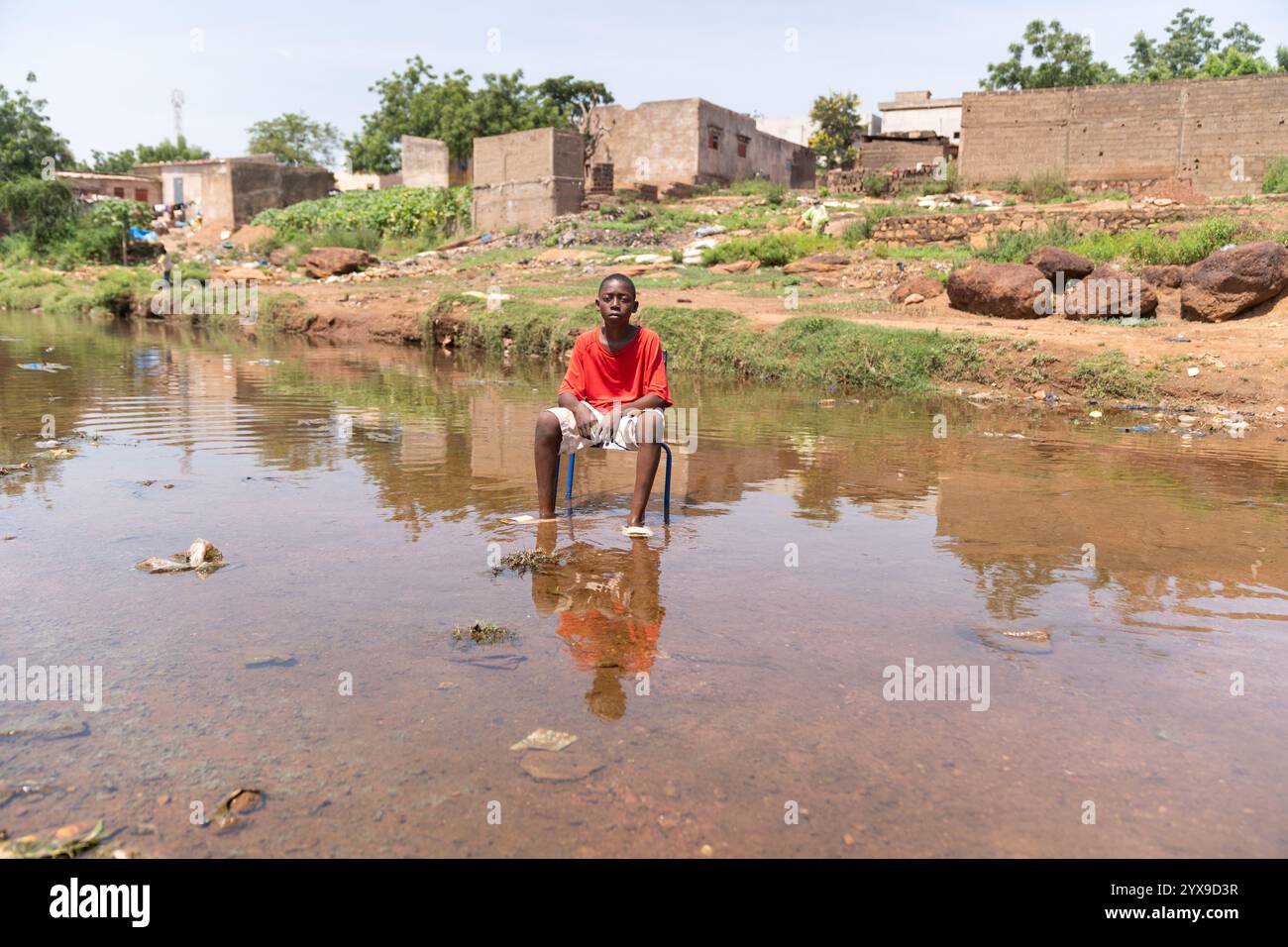 Young African boy sitting on a chair in the middle of a flooded area ...